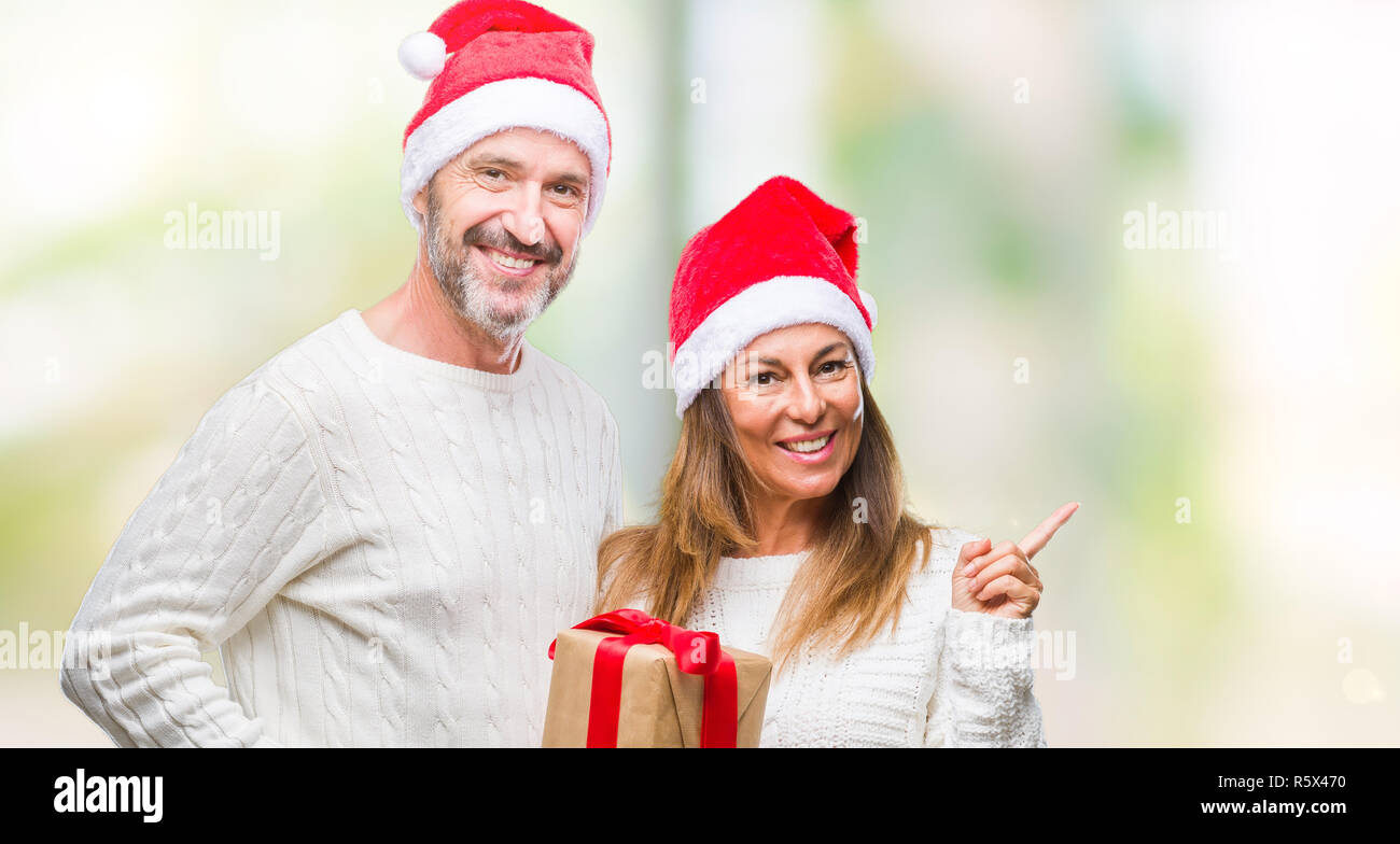 Middle age hispanic couple wearing christmas hat and holding gift over ...