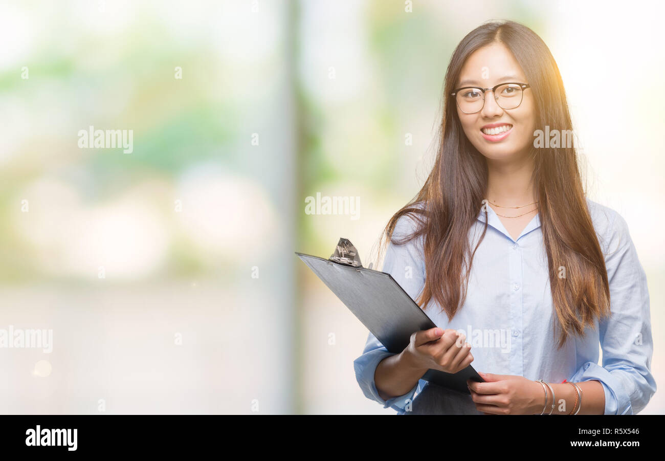 Young asian business woman holding clipboard over isolated background ...