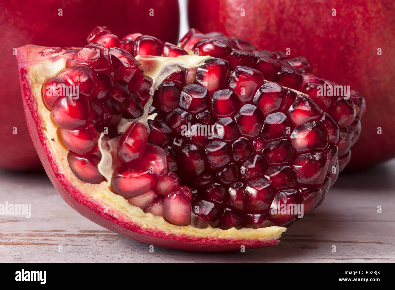 Fruit of red pomegranate on wooden plank, half with seeds, close up ...