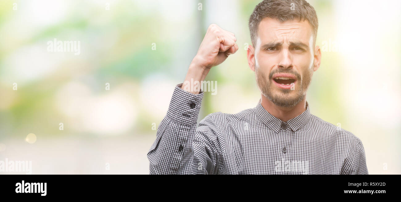 Young hipster man angry and mad raising fist frustrated and furious ...