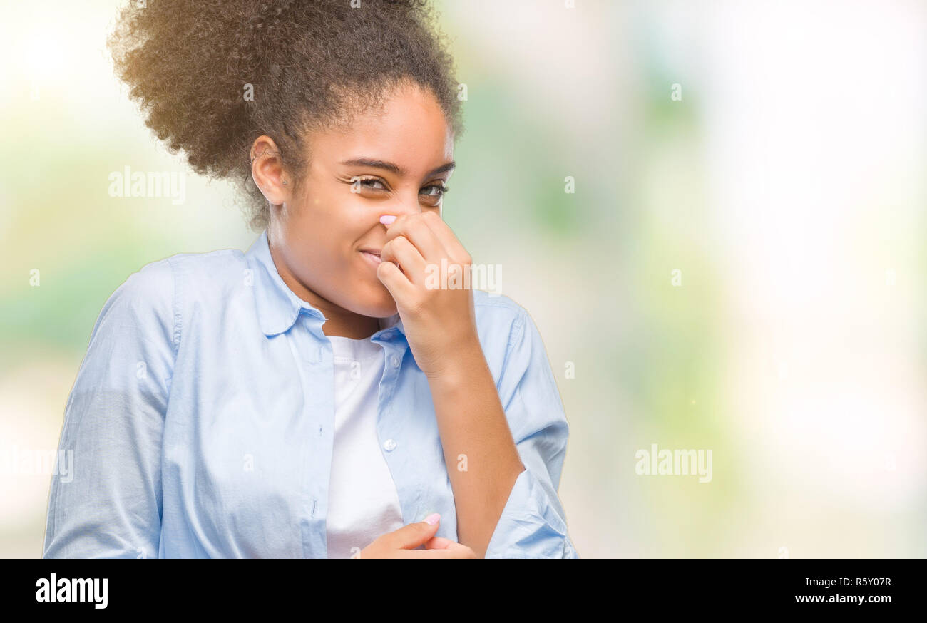 Young afro american woman over isolated background smelling something ...
