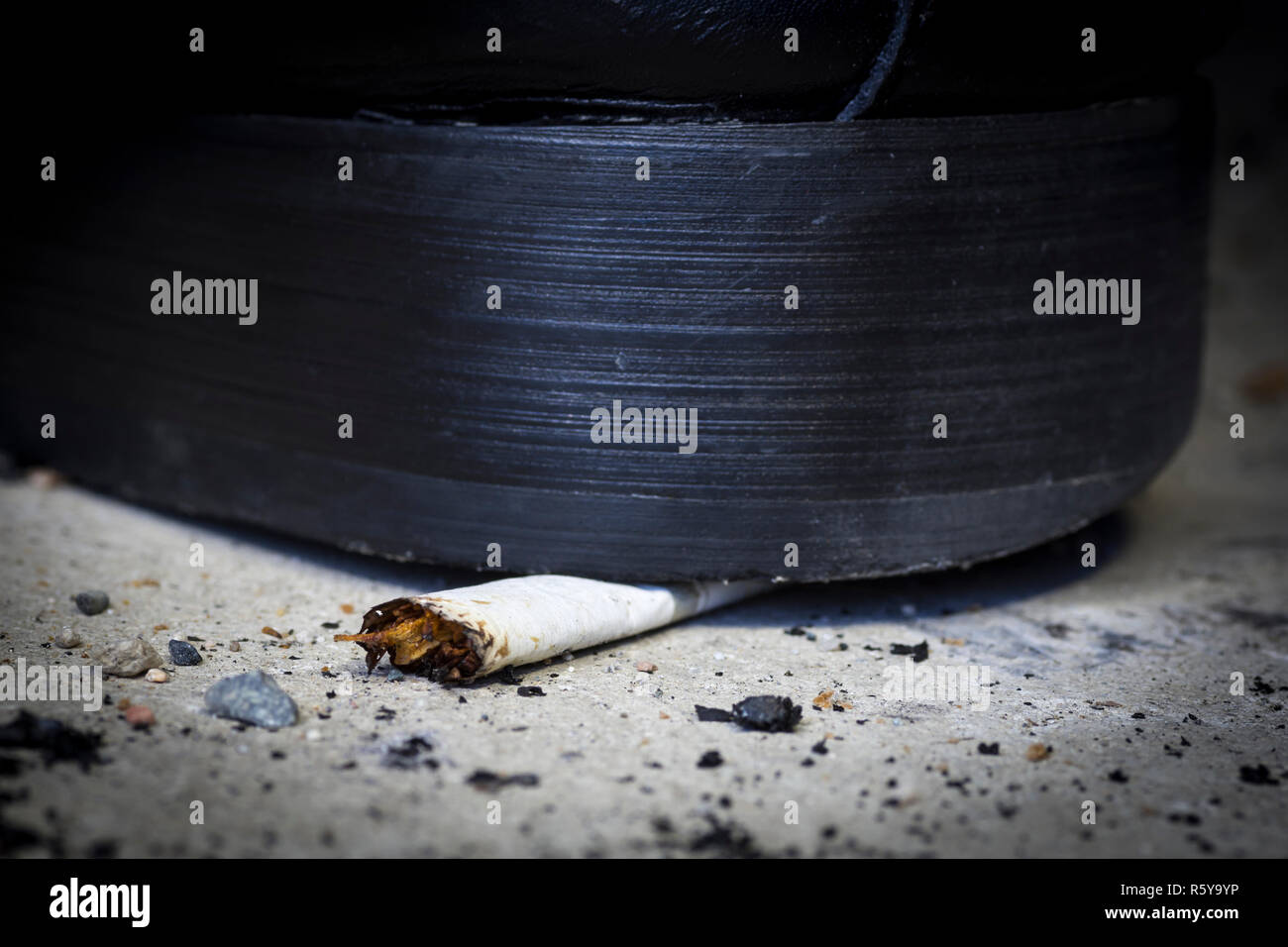A black leather shoe stepping on cigarettes tobacco butts on the floor ...