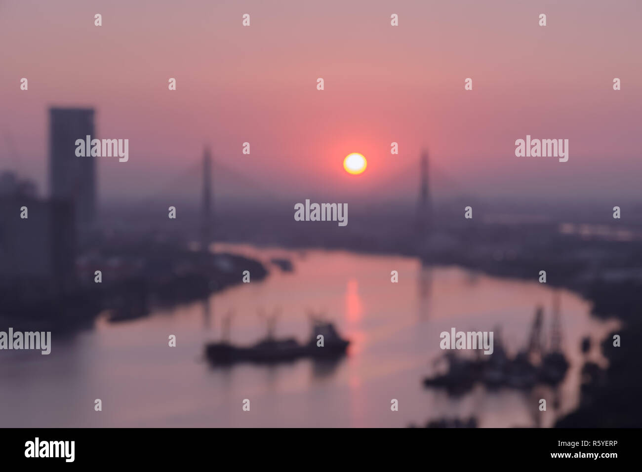 Abstract blurred photo of riverside cityscape with sunrise over bridge ...