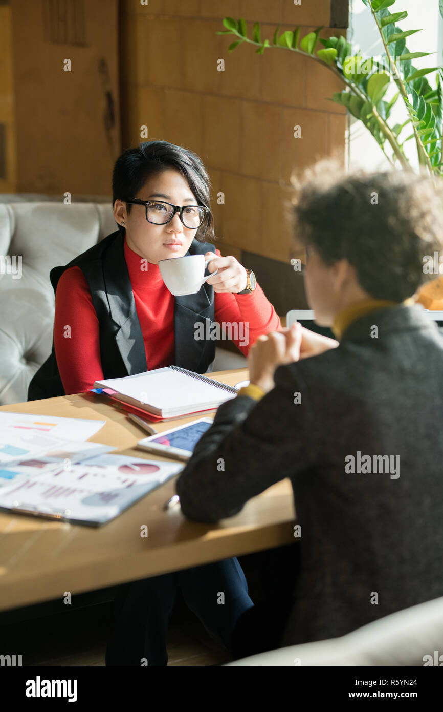 Serious Asian lady talking to business partner in cafe Stock Photo - Alamy