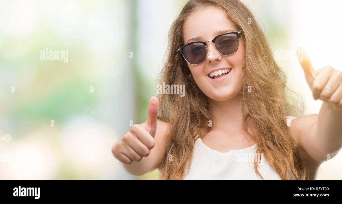 Young blonde woman wearing sunglasses approving doing positive gesture ...