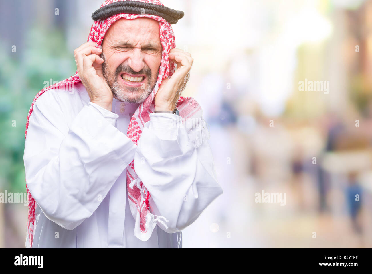 Senior arab man wearing keffiyeh over isolated background covering ears ...