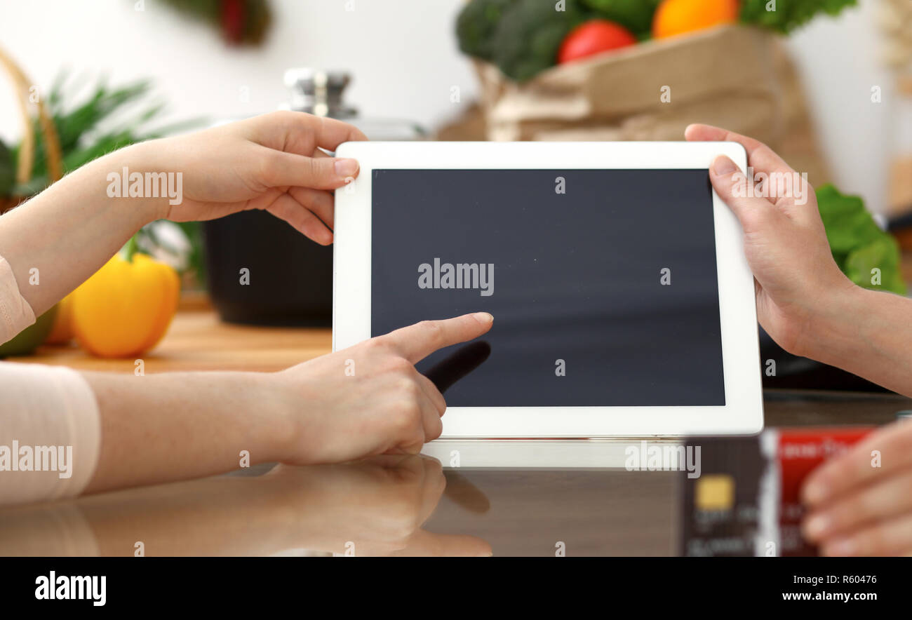 Close-up of human hands using tablet or touch pad. Two women in kitchen ...