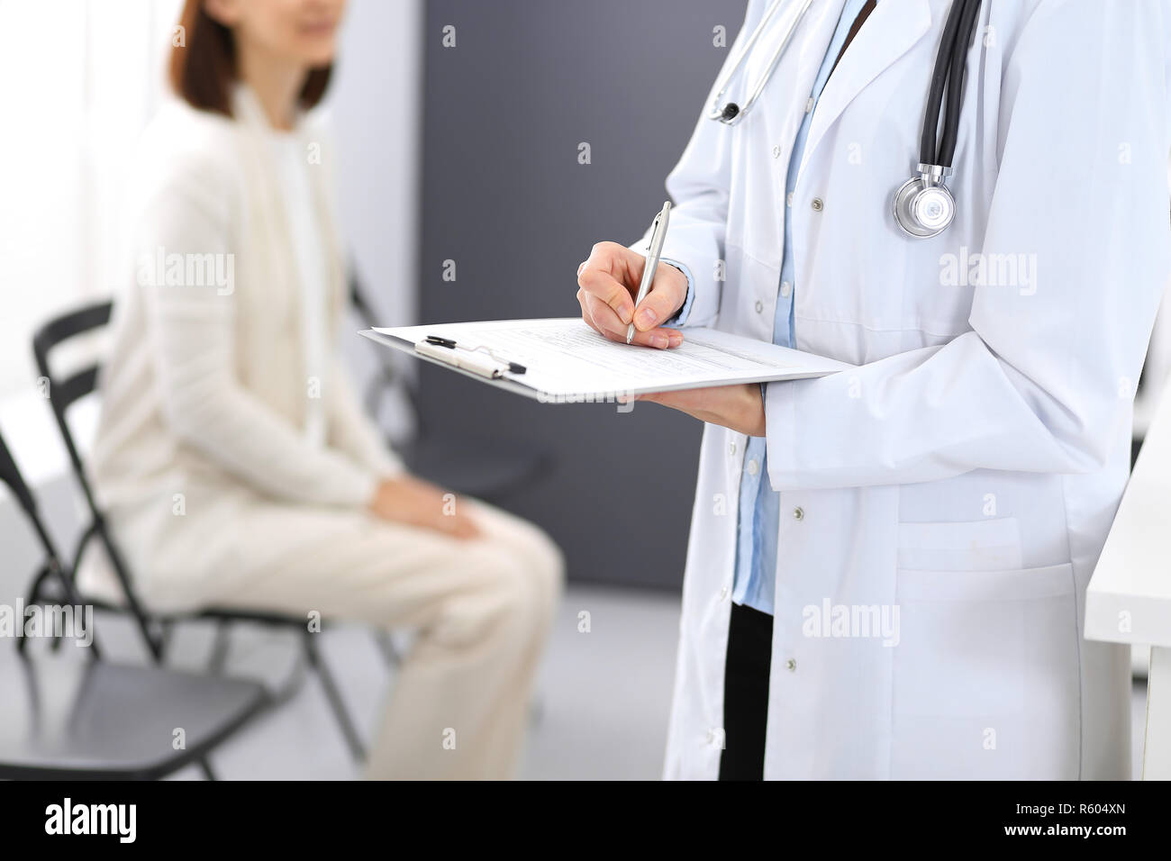 Doctor woman filling up medical form while standing near reception desk ...