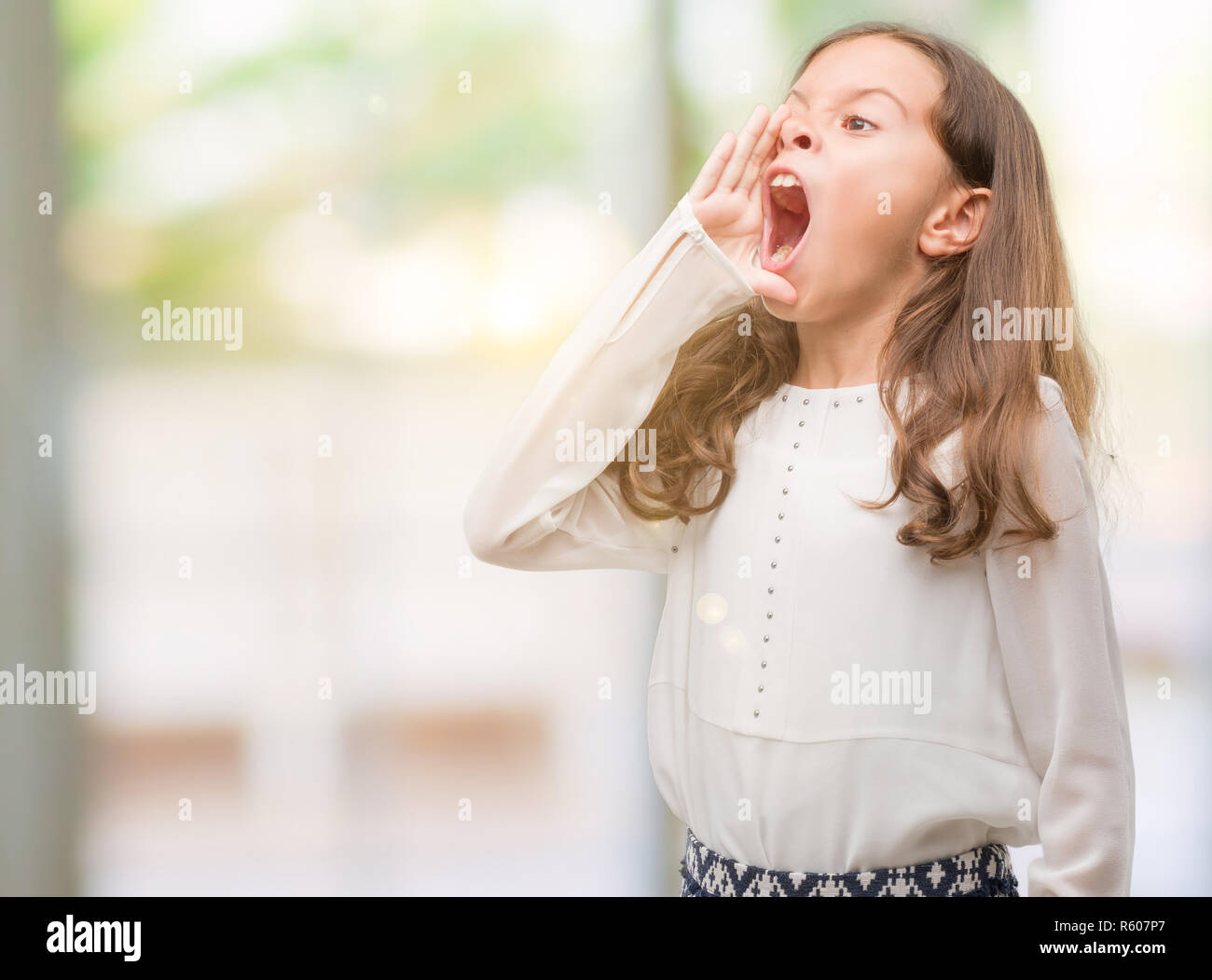 Brunette hispanic girl shouting and screaming loud to side with hand on ...