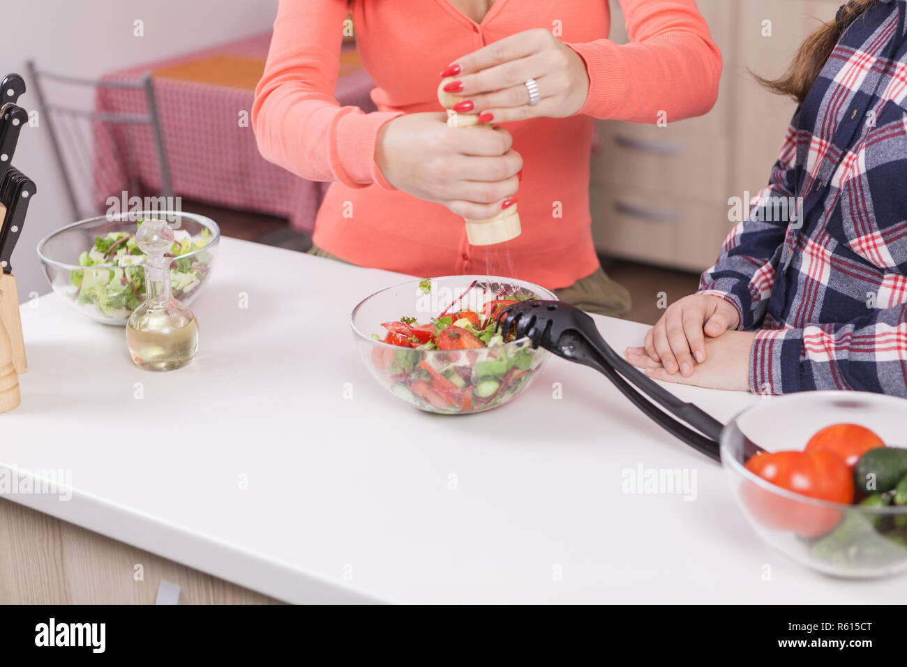 Mother pouring salt over green salad in kitchen. Secret ingredient ...