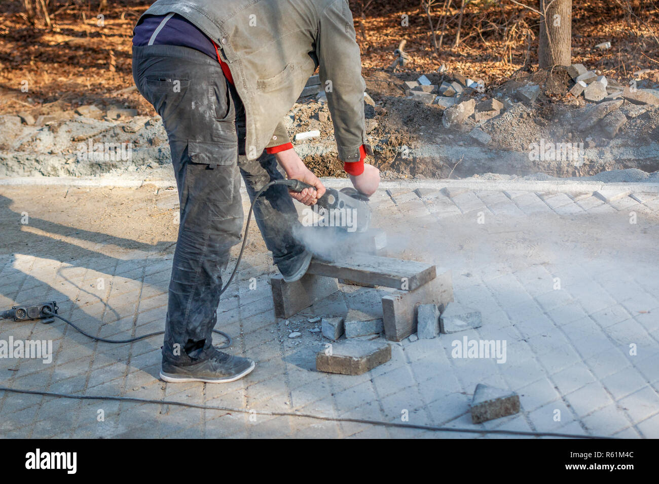 A worker prepares a sidewalk for paving a footpath. Cuts a brick with ...