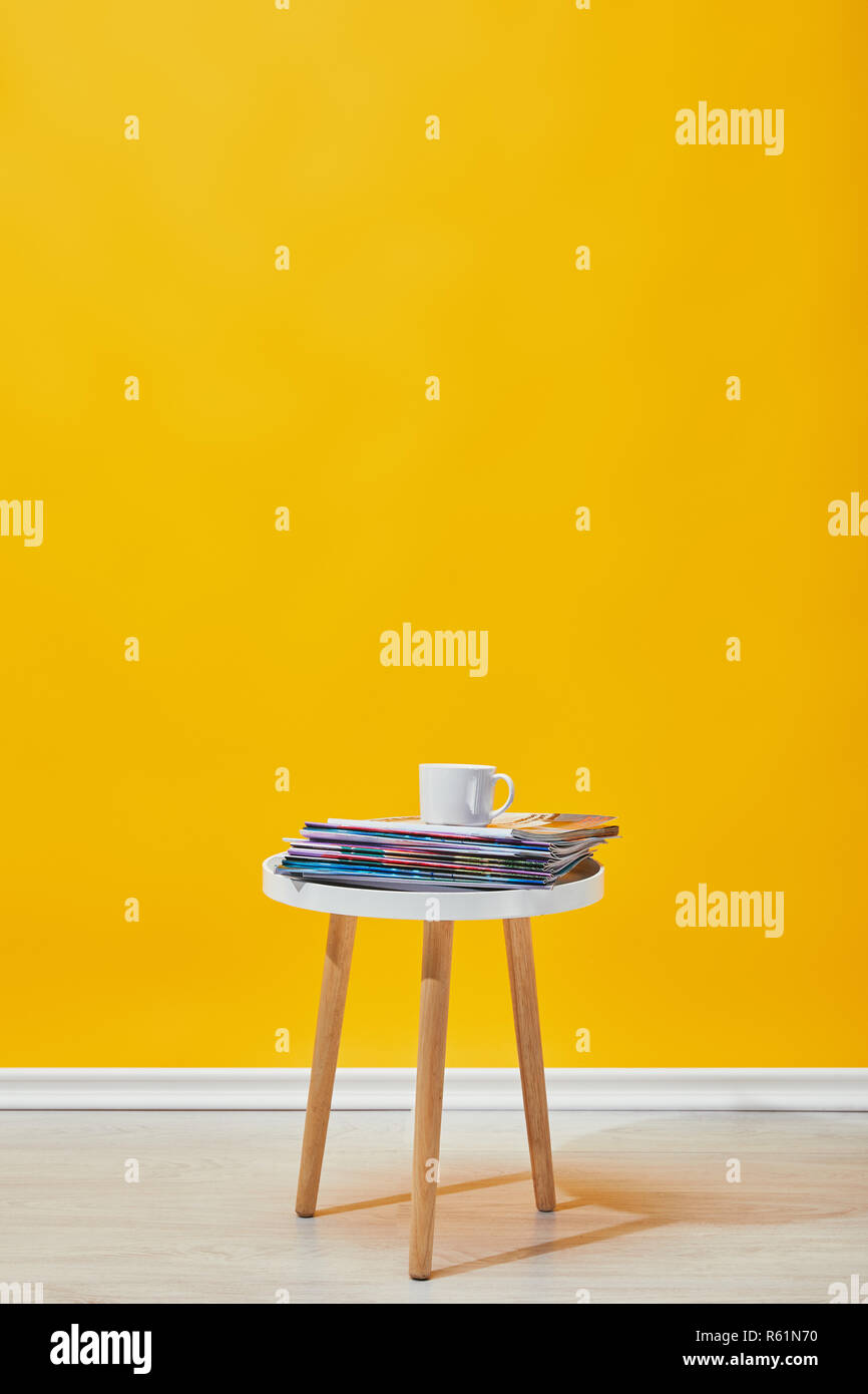 Little coffee table with journals and cup of coffee near yellow wall ...