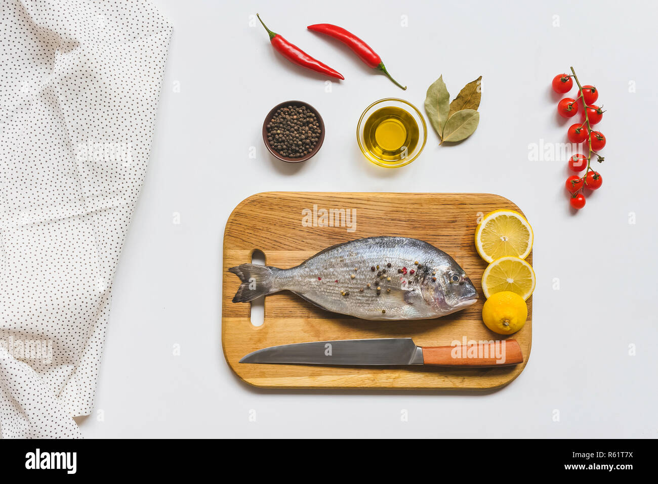 elevated view of uncooked fish and various ingredients on white table ...