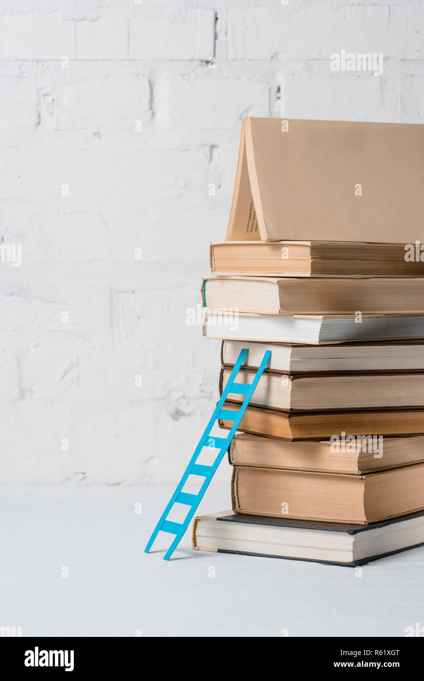 pile of books and small blue step ladder near white brick wall Stock ...