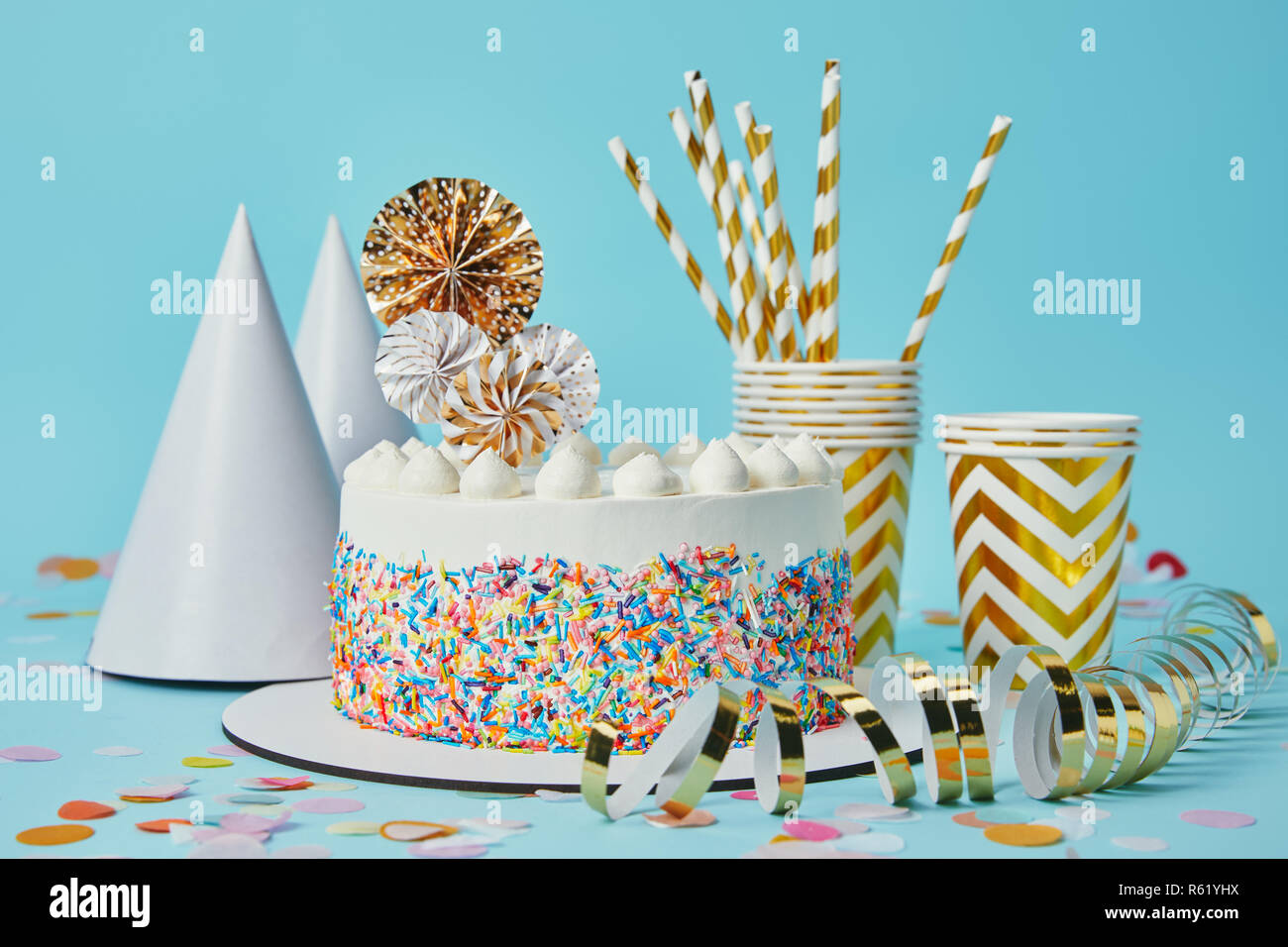 Cake, party hats, plactic cups, golden paper streamer and drinking ...