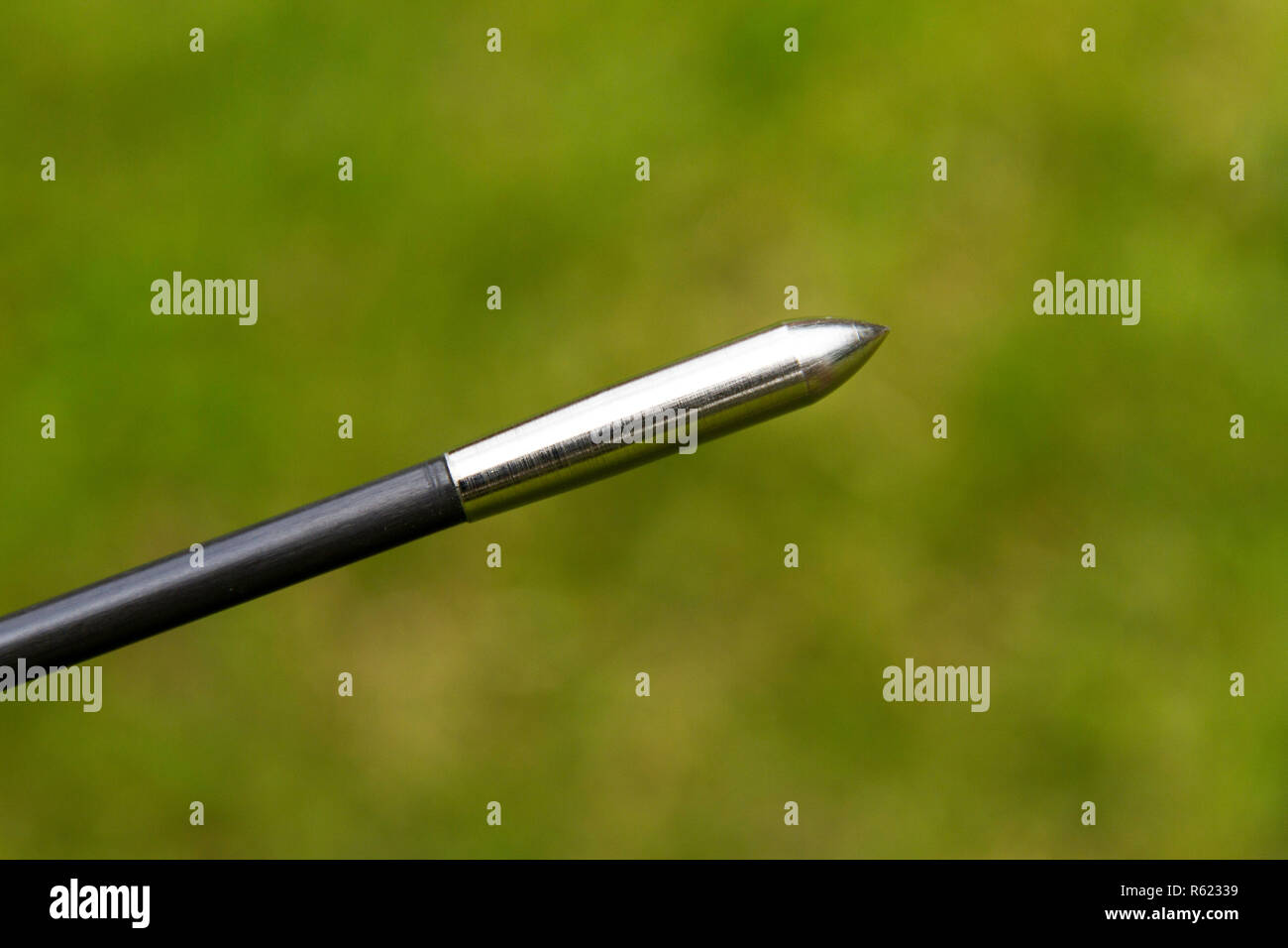 metal tip of an arrow in front of green background Stock Photo - Alamy