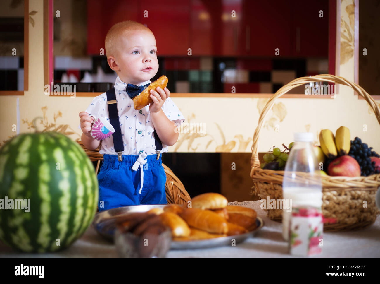 Little boy eating a pie in the kitchen at the table. Shooting in the ...