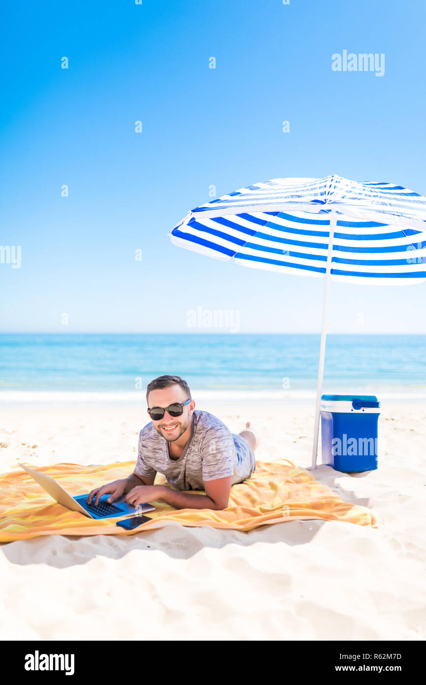 Young man using a laptop computer on the beach under solar umbrella ...