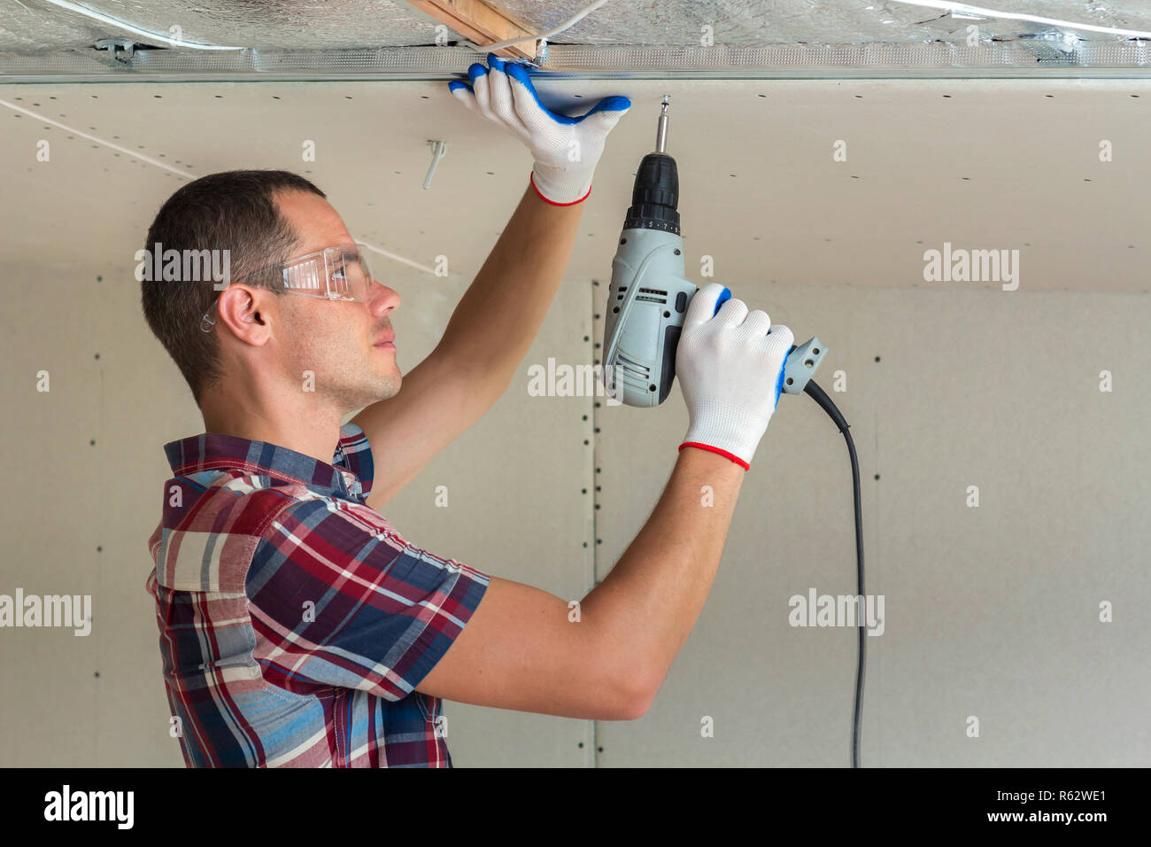 Young man in goggles fixing drywall suspended ceiling to metal frame ...