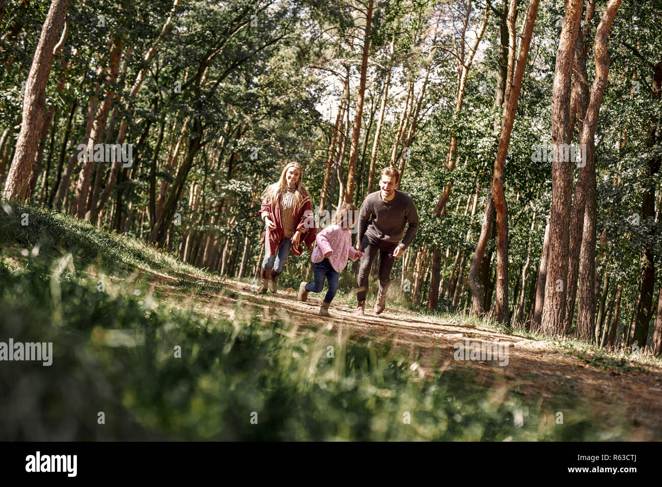 Happy parents with their daughter hold hands and run at forest path ...