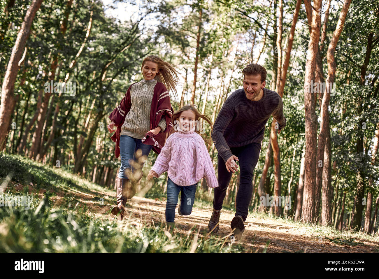 Happy parents with their daughter hold hands and run at forest path ...