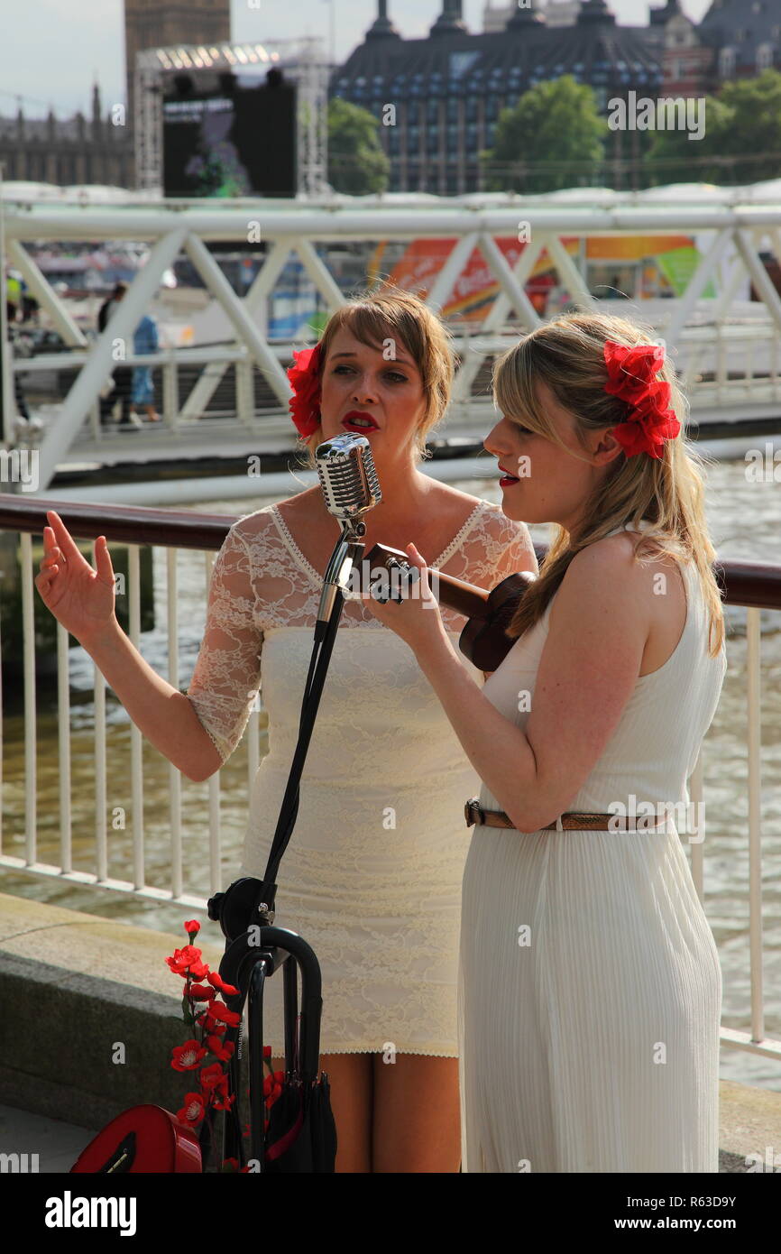 Street performers in London. Two girls singing by the river Thames in ...