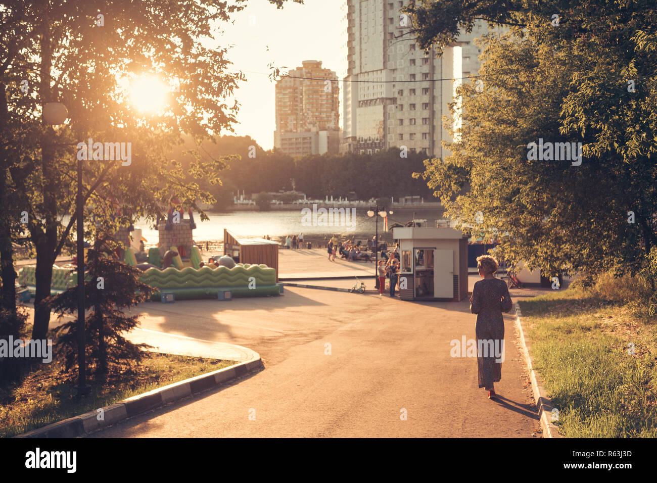 Woman walking along the road to the river bank on the sunset in a ...