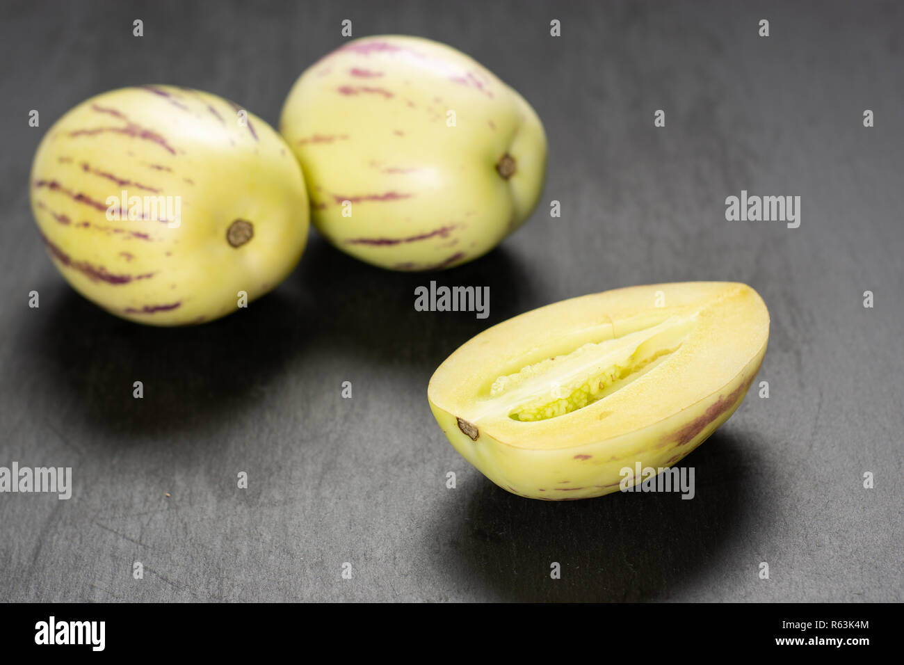 Group of two whole one half of fresh striped pepino melon on grey stone ...