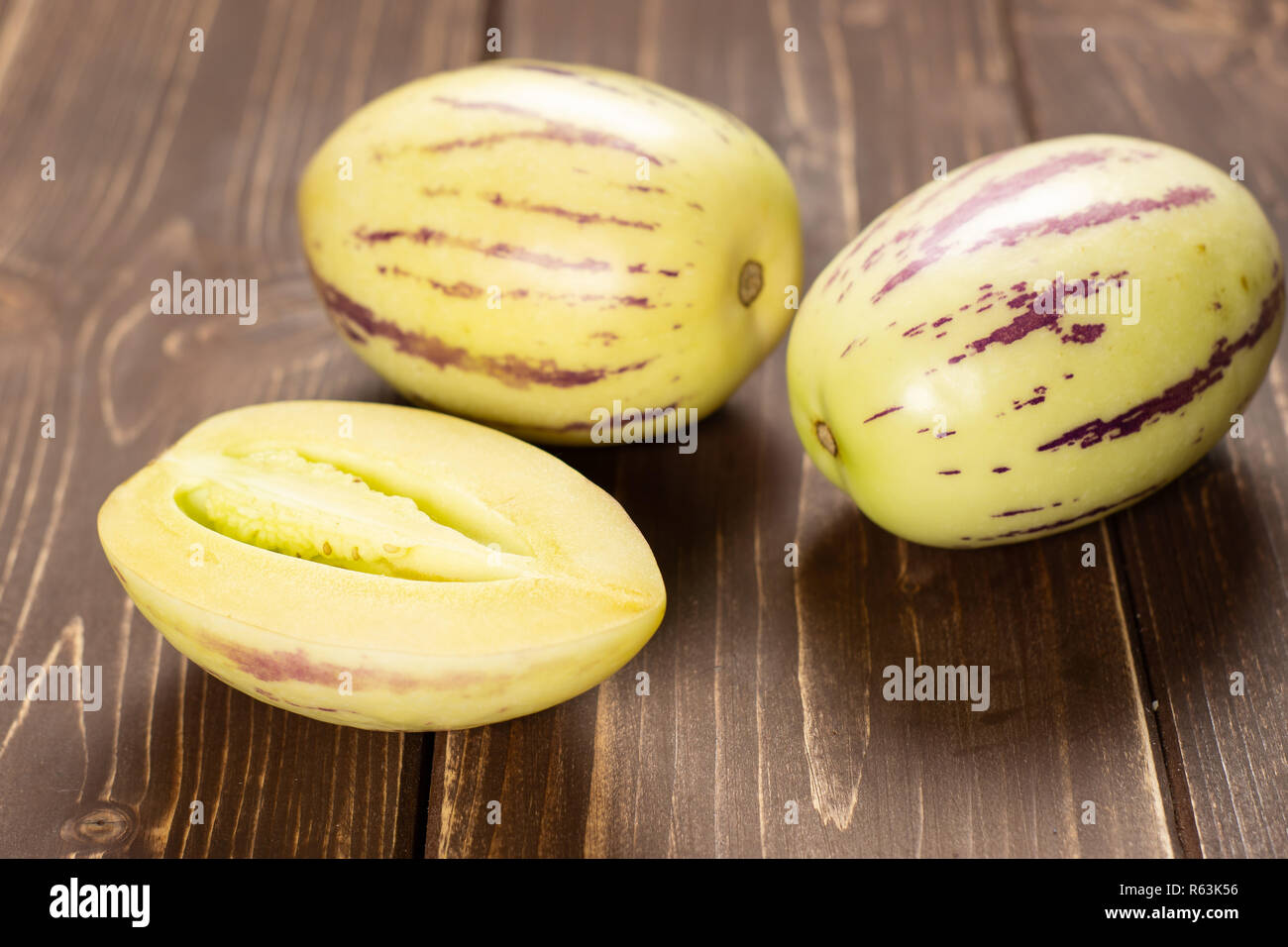 Group of two whole one half of fresh striped pepino melon on brown wood ...