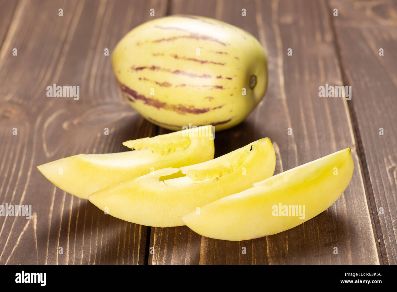 Group of one whole three slices of fresh striped pepino melon on brown ...