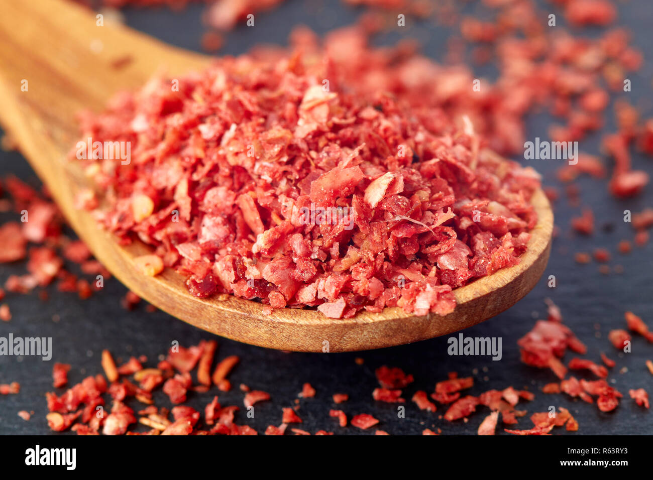 Dried chopped chili pepper in wooden spoon on black rustic background ...