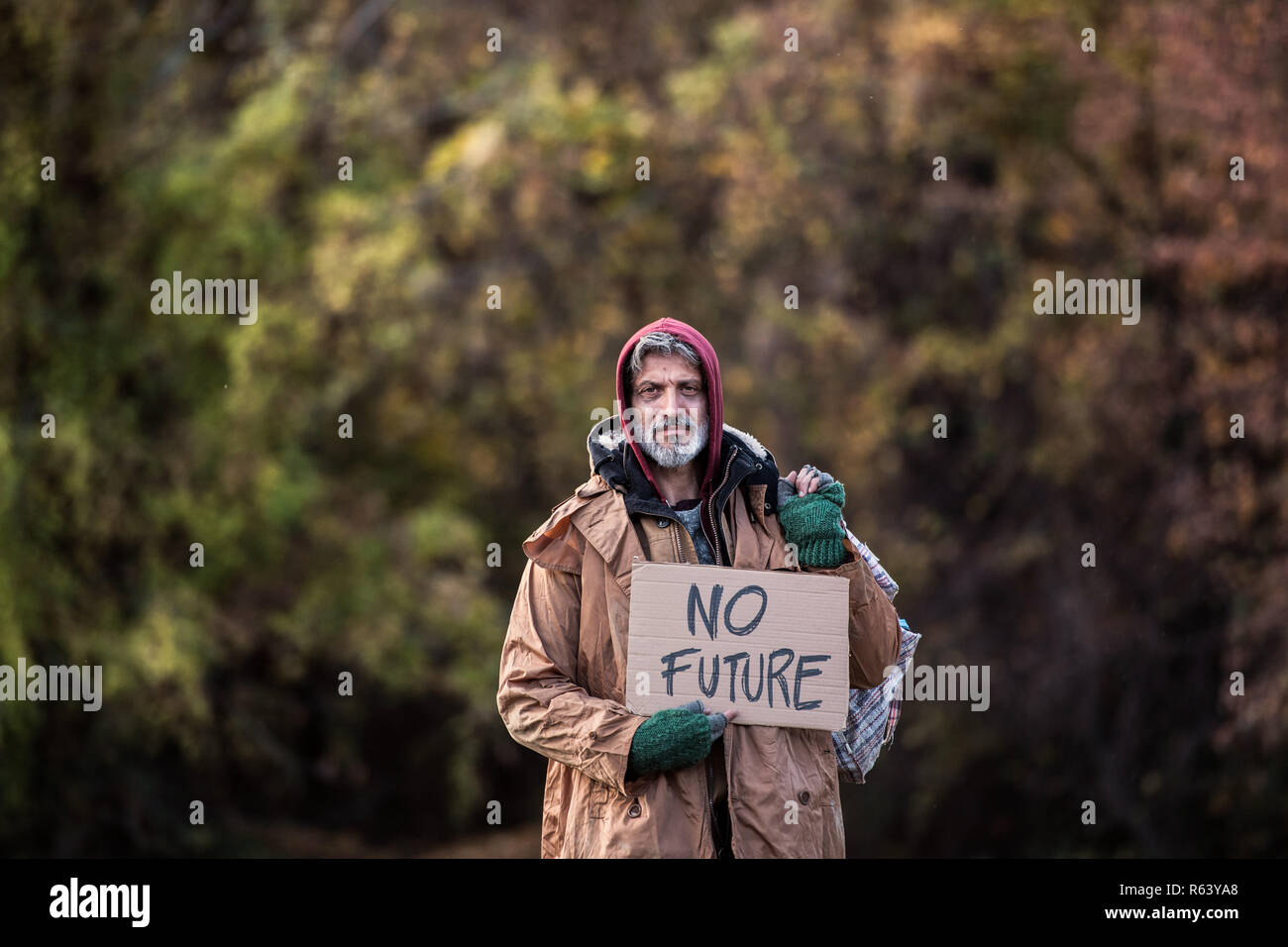 Homeless beggar man standing outdoors in park, holding bag and ...