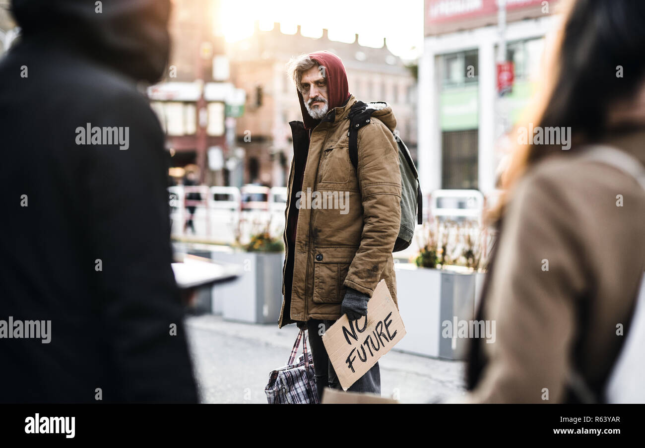 Homeless beggar man walking outdoors in city, holding bag and cardboard ...