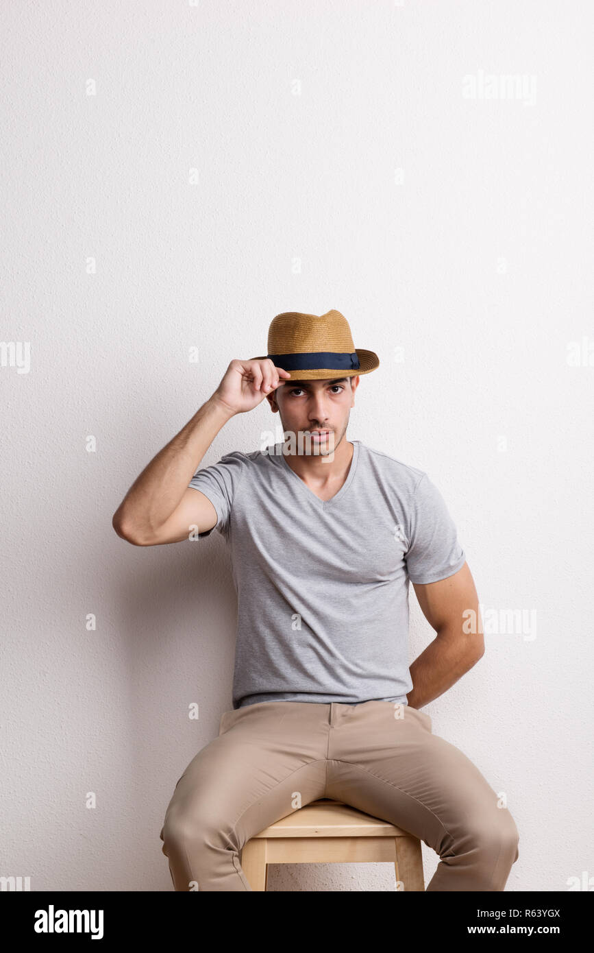 A confident hispanic young man with hat sitting on a stool in a studio ...