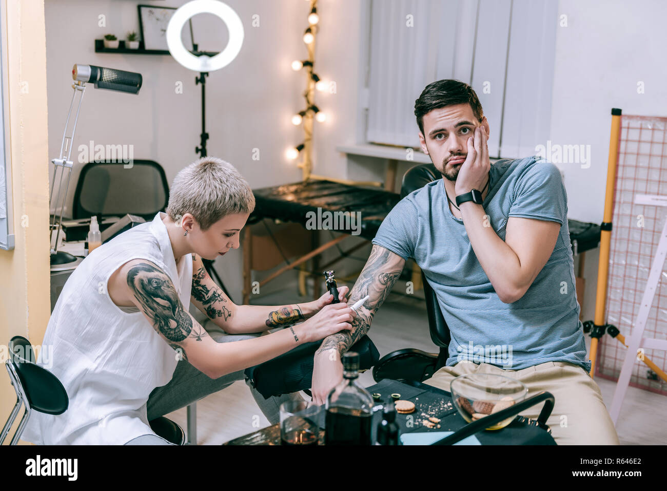 Tired good-looking customer of tattoo master finishing his tattoo Stock ...