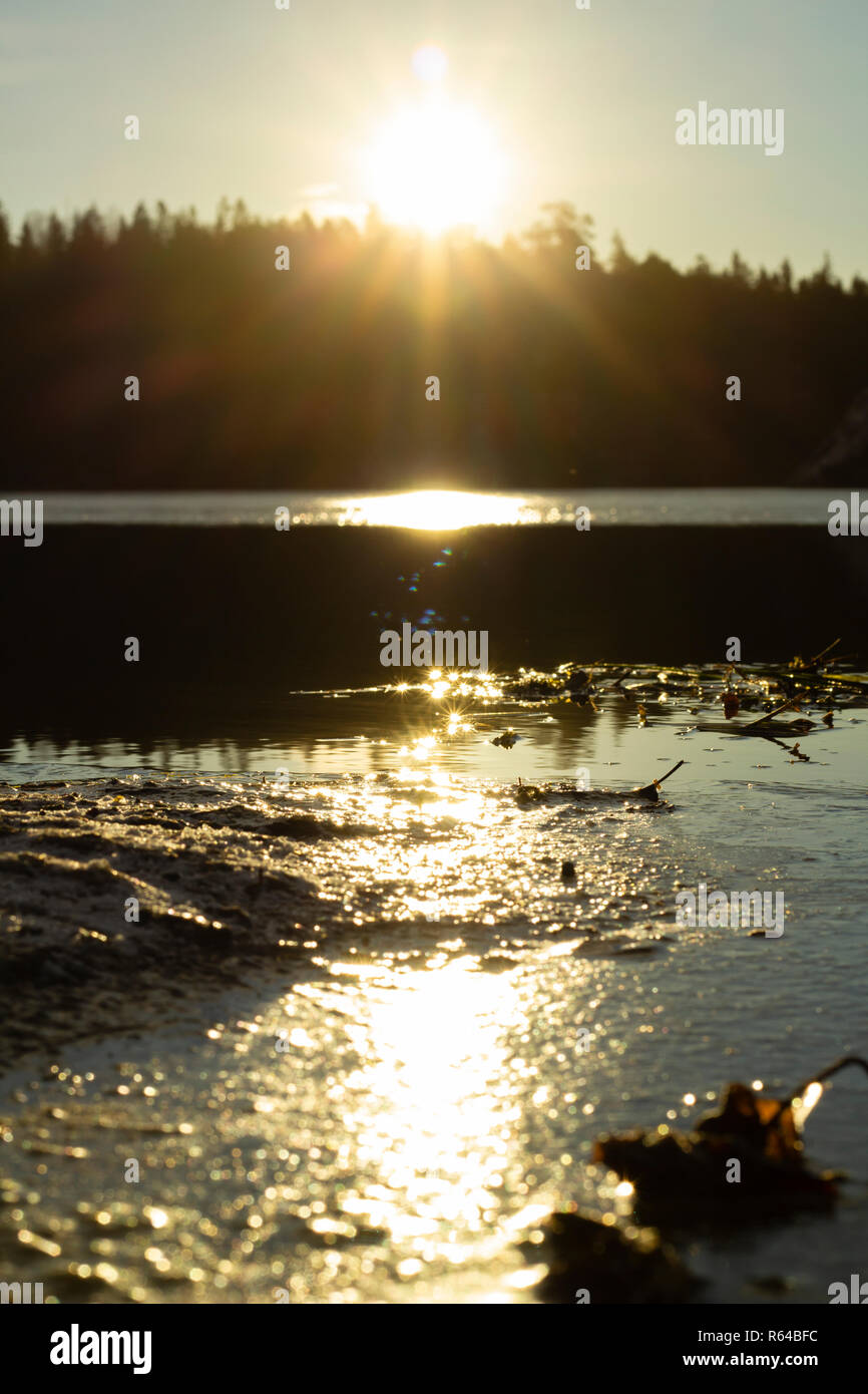 Newly risen sun is reflected on a partly frozen lake, creating a line ...