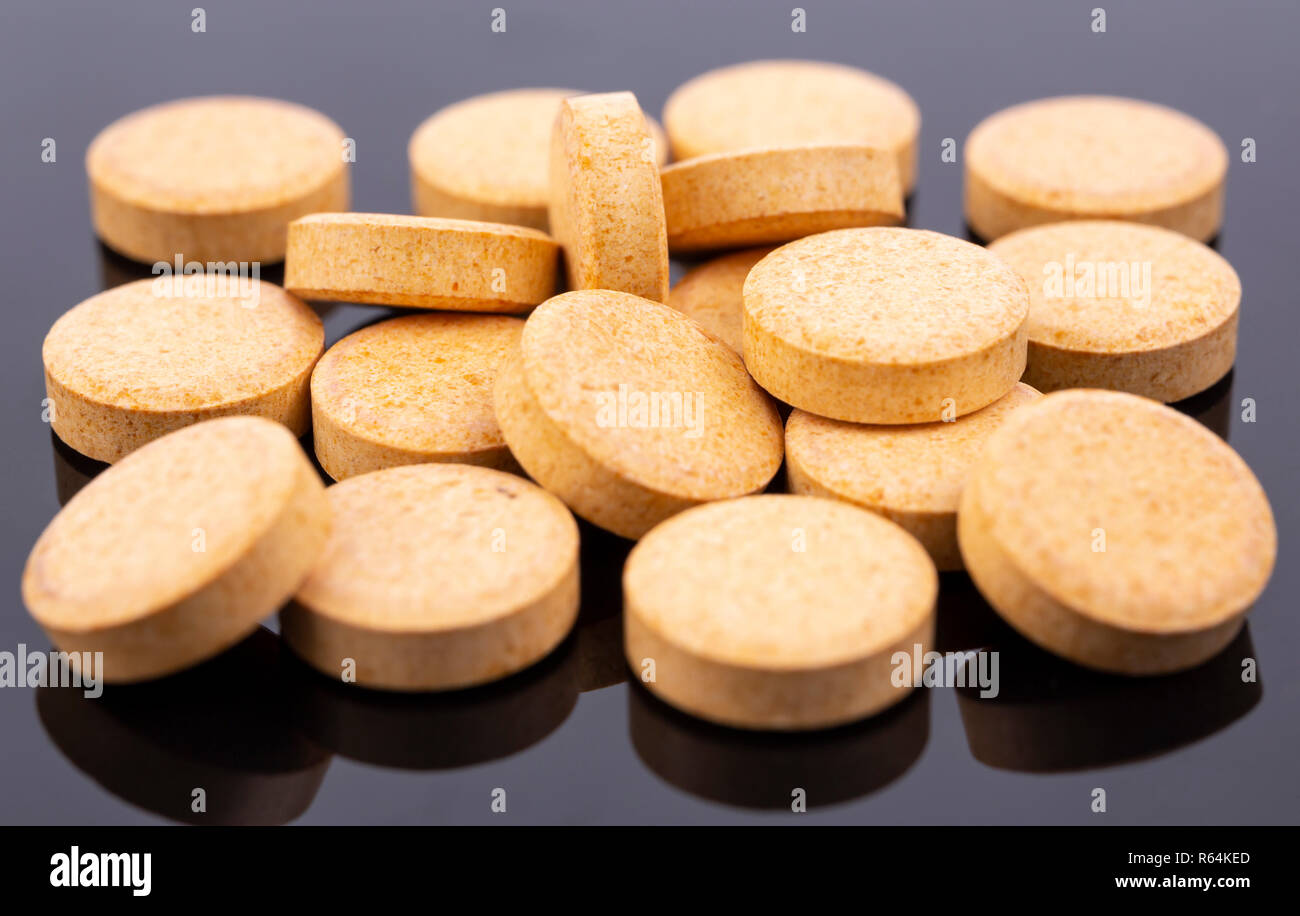 Yellow pills isolated on black reflective surface. Global ...