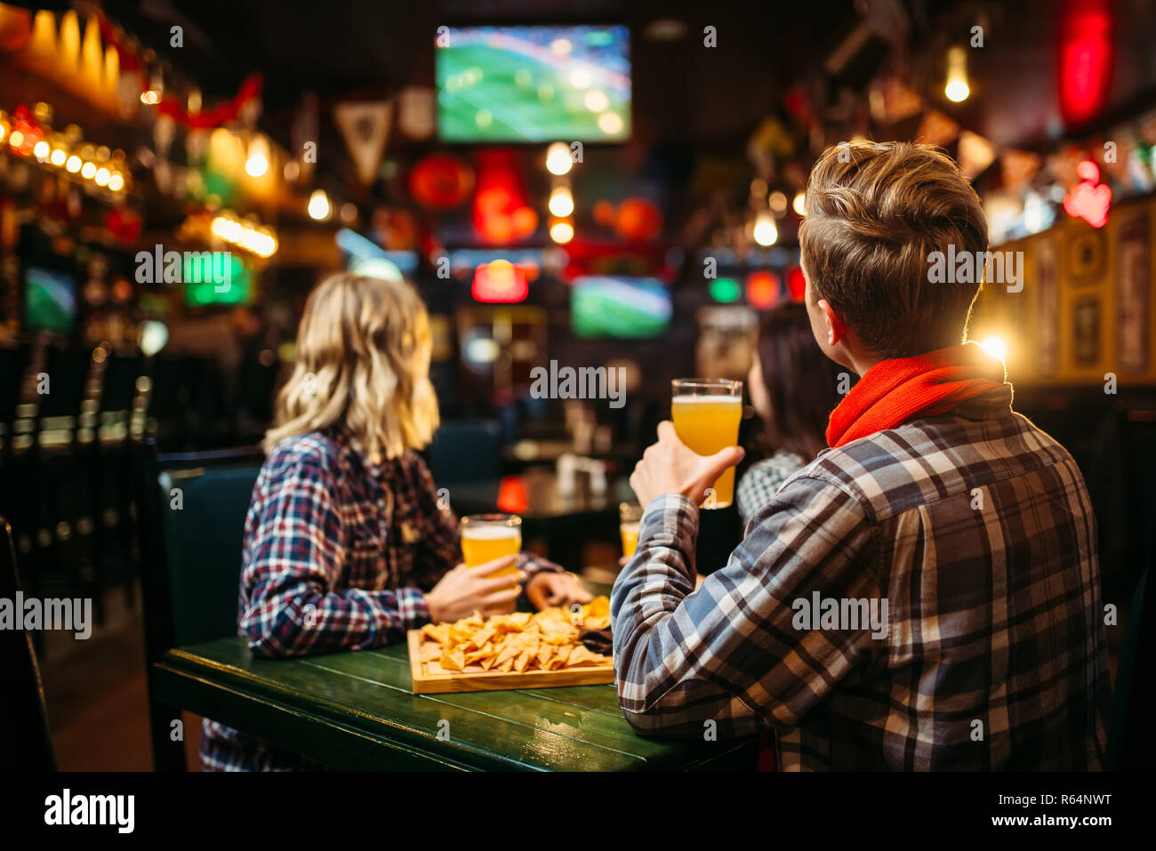 Football fans watching match and drinks beer at the table in sports bar ...