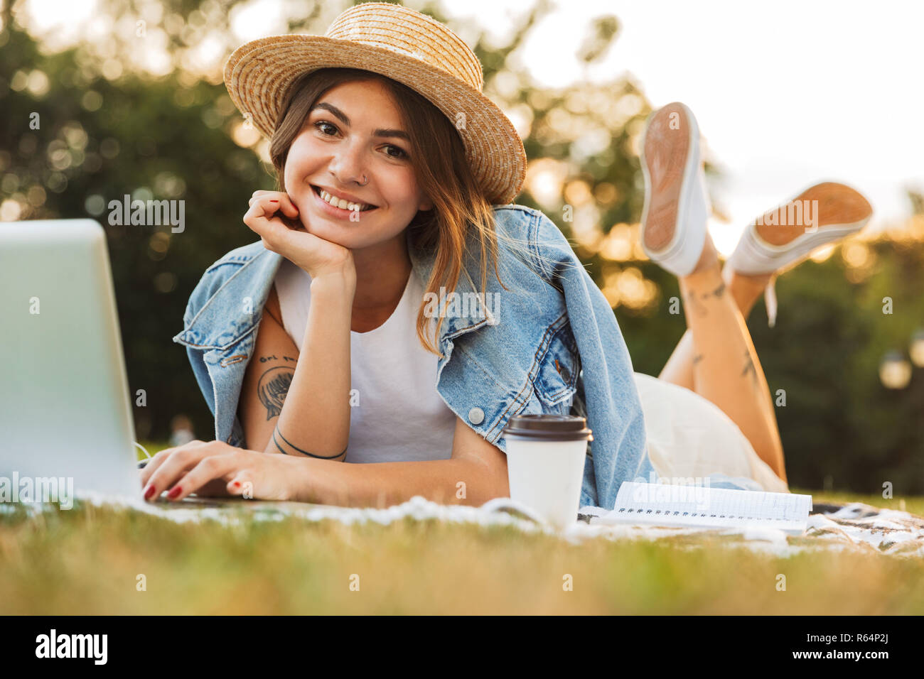 Cheerful young girl laying on grass at the park, using laptop computer ...