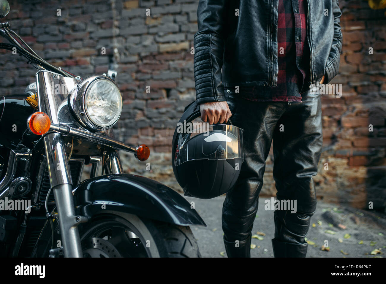 Biker in leather jacket with helmet in hand near classical chopper ...