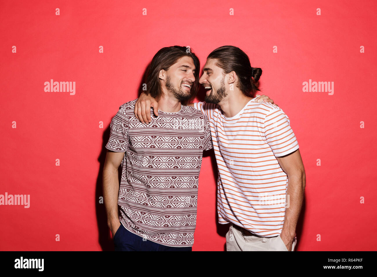 Portrait of two smiling twin brothers standing isolated over red ...