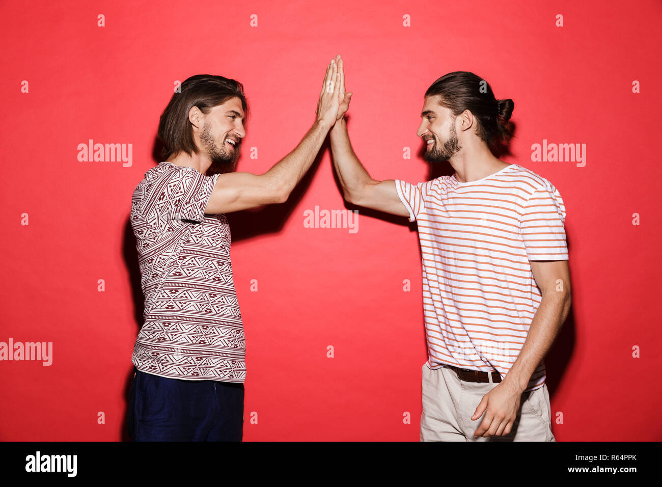 Portrait of two smiling twin brothers standing isolated over red ...