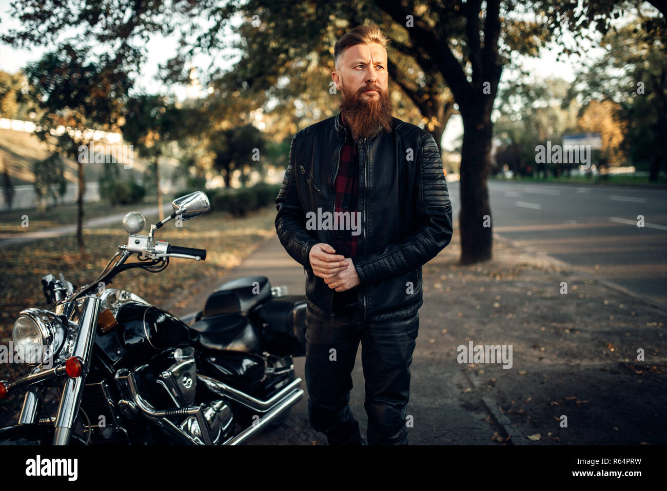 Biker in leather jacket standing near black chopper. Vintage bike ...
