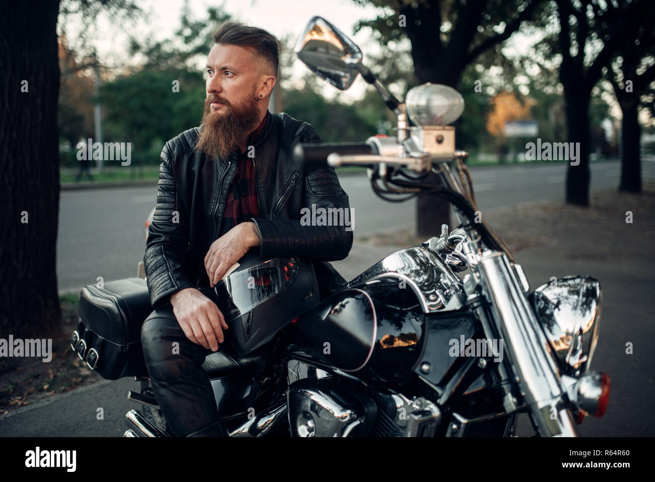 Baerded biker poses on chopper leaning on a helmet. Vintage bike, rider ...
