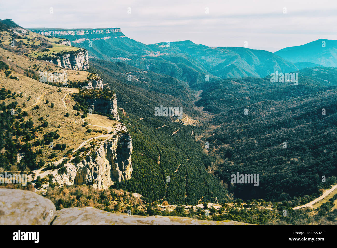 A steep cliff seen from above with a vast expanse of fields full of ...
