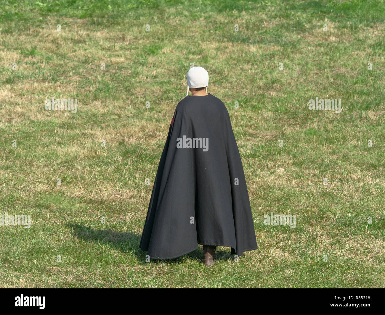 Rear view of man in medieval cloak and cap religious clothing walking ...