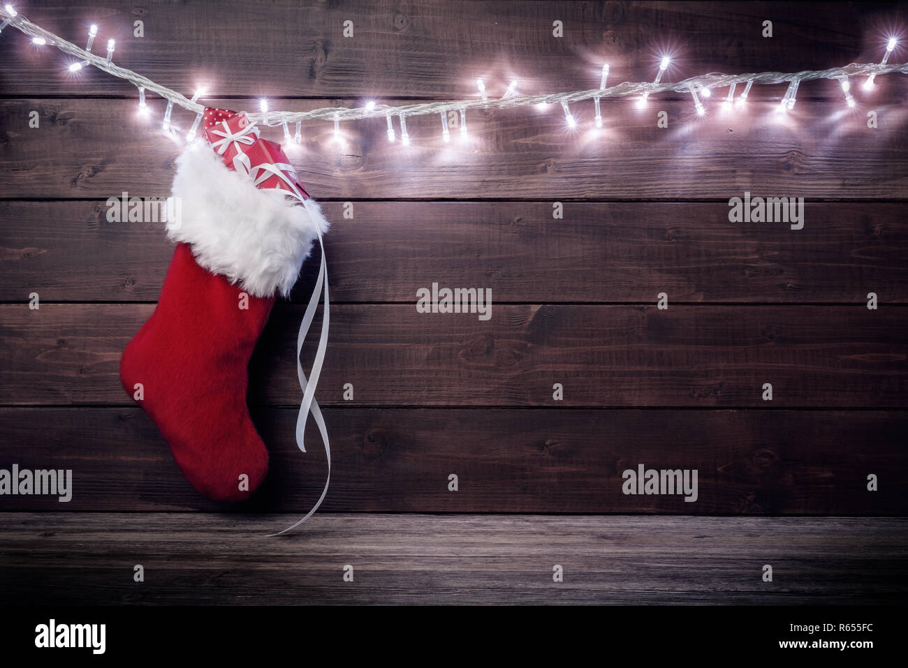Red Santa stocking with gift boxes hanging on glowing garland over ...