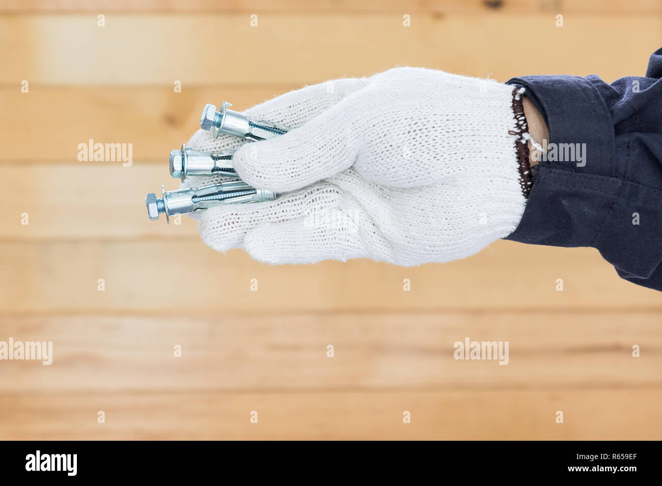 Hand in glove holding metal anchor bolts Stock Photo - Alamy