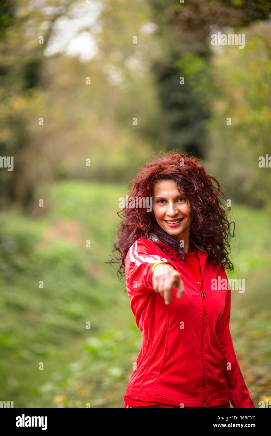 Girl in red gym suit smiling in garden ponting to viewer. long red hair ...