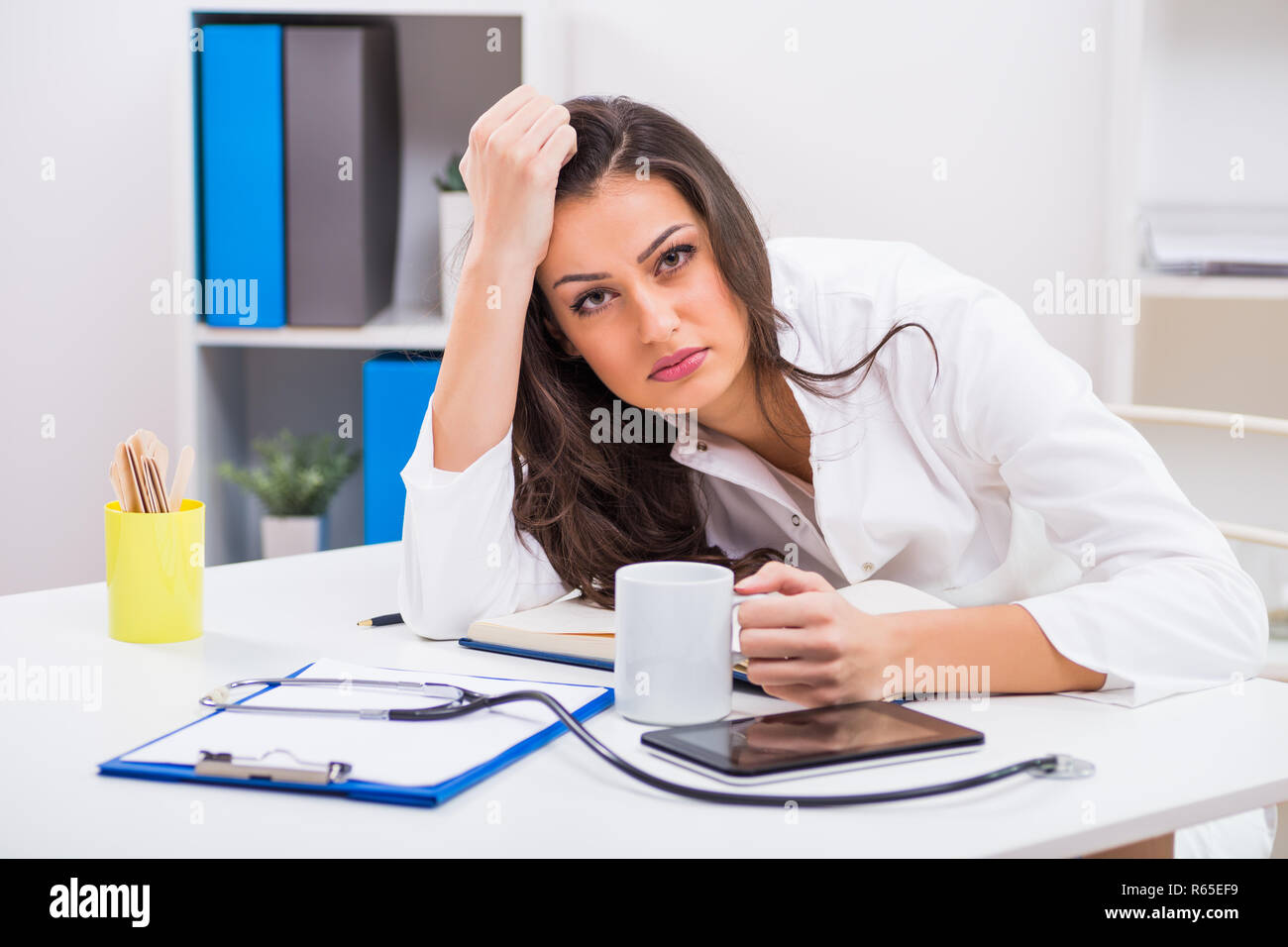 Tired female doctor is drinking coffee while working at her office ...